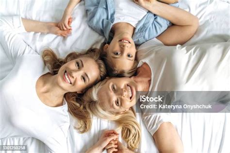 쾌활한 행복한 할머니 딸과 손녀가 침대에 누워 카메라를 보고 미소를 지으며 사진을 찍었습니다 가족 관계와 가치 딸에 대한 스톡