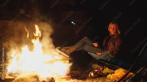 A Young Guy And A Girl Are Sitting On Folding Chairs By The Fire And