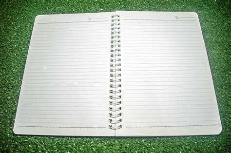 줄이 그어진 페이지가 있는 열린 나선형 공책이 푸른 잔디 위에 놓여 있습니다 노트북은 비어 있고 쓰기 준비가 되어 있어 메모 작성 저널링 또는 스케치에 이상적입니다 0명에