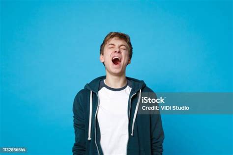 스튜디오에서 파란색 벽 배경에 고립 된 눈을 닫힌 비명을 유지 캐주얼 옷에 미친 젊은 남자의 초상화 사람들은 진심으로 감정 라이프 스타일 개념입니다 복사 공간을 모의 합니다
