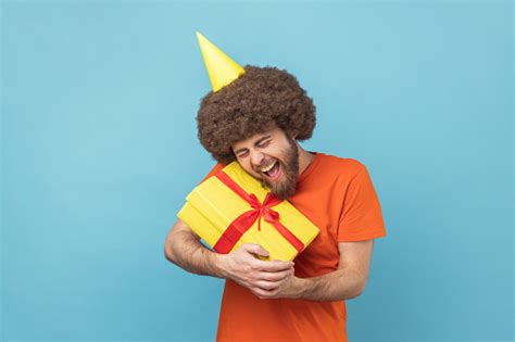 파티 콘에 만족한 남자는 노란색 선물 상자를 포용하고 선물하게되어 기쁩니다 스튜디오 촬영에 대한 스톡 사진 및 기타 이미지