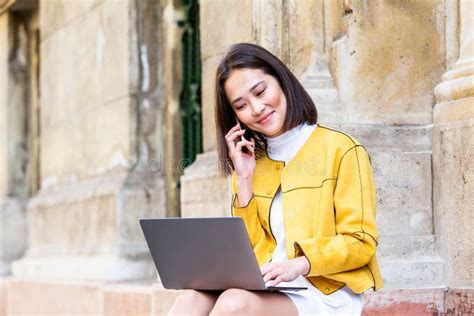 Smiling Asian Woman Working On Laptop Computer While Sitting On The Floor And Talking On Her
