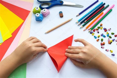Las manos de los niños hacen origami pájaro de papel rojo
