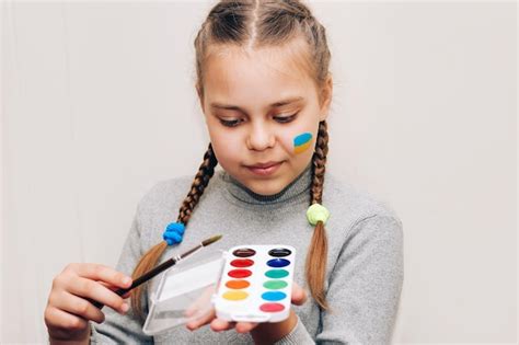 Портрет девушки сине желтым рисунком флага Украины нарисован на щеке красками с кистью в руках