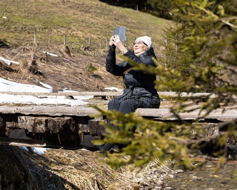An Adult Woman Sits On A Wooden Bridge Legs Dangling And Takes
