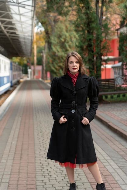 Mulher de meia idade usa casaco retrô preto no estilo dos anos e está na plataforma da