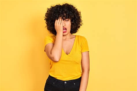 고립 된 노란색 배경 하품 피곤 한 손으로 반 얼굴 눈과 입을 덮고 피곤 위에 서 있는 곱슬 머리를 가진 젊은 아랍 여성 얼굴은