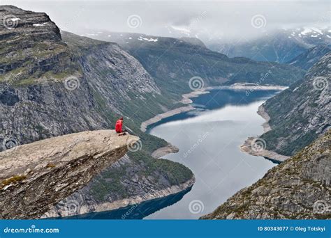 Человек при камера сидя на утесе языка ` S тролля утеса Trolltunga