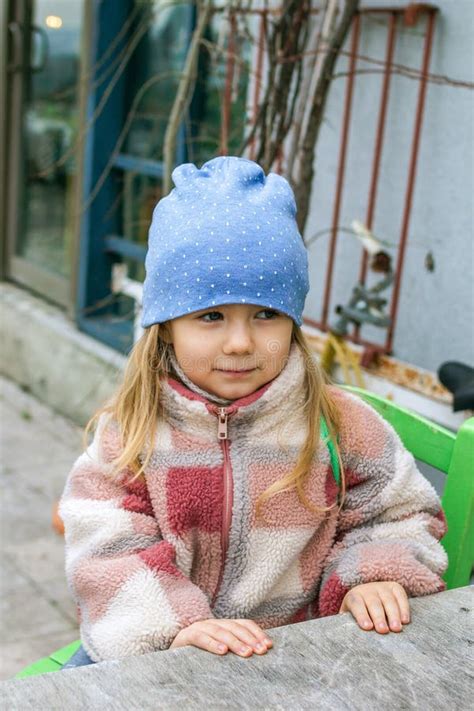 A Young Girl With Blonde Hair Smiles In A Blue Hat With White Polka Dots A Colorful Jacket And