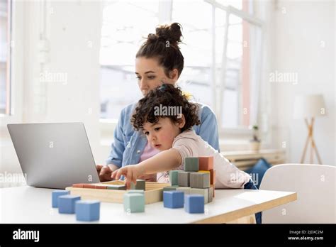 Mother Working From Home Using Laptop While Daughter Is Playing With Buiilding Blocks Stock