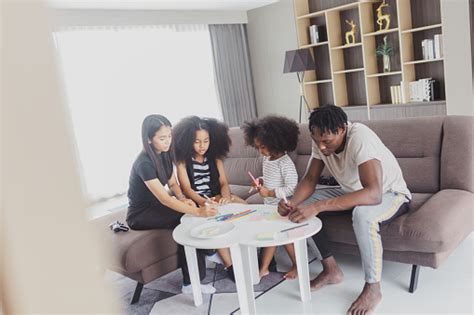 젊은 아시아계 미국인 가족 부모와 어린 딸이 집에서 함께 그림을 그립니다 아시아계 미국인 가족과 아빠가 거실에서 아이와 함께 그림을 그리고 연필을 사용하고 재미 있고