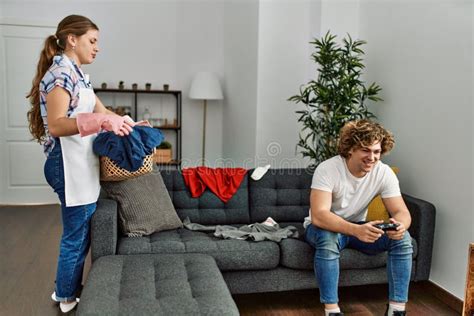 Woman Doing Laundry While Man Plays Video Game At Home Stock Photo