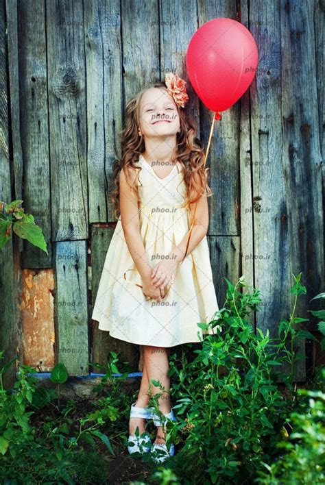 عکس با کیفیت دختر زیبا ایستاده در کنار دیوار چوبی با یک بادکنک قرمز در