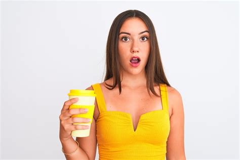 젊은 아름 다운 여자 마시는 종이 유리 의 테이크 아웃 커피 위에 고립 된 흰색 배경 에 무서워 충격으로 충격 두려움과 두려움 표정으로 흥분 갈색 머리에 대한 스톡 사진 및