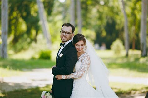 아름 다운 결혼식 Photosession입니다 검은 양복과 흰색 레이스 드레스와 긴 깃털 베일 부케 미소 Weathery 화창한 날에 큰 녹색 정원에서 포옹에에서 그의 신부