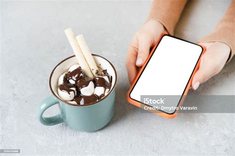 마시멜로와 여성의 손이 뿌려진 뜨거운 코코아 머그잔은 빈 흰색 화면으로 스마트폰을 들고 복사 공간을 확보합니다 위에에 대한 스톡 사진 및 기타 이미지 Istock