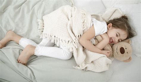 Uma Linda Menina Está Dormindo Em Uma Cama Com Um Ursinho De Pelúcia
