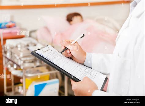 Doctor Writing On A Medical Chart With Fake Patient In Hospital Room