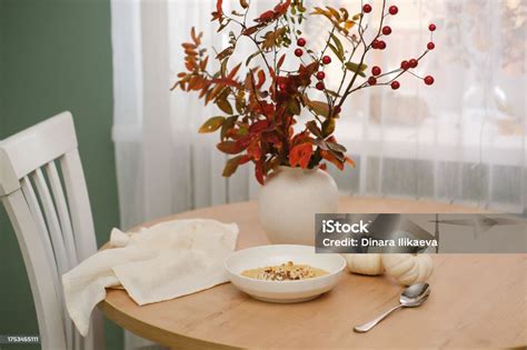 아침 식사 테이블 호박과 견과류를 곁들인 오트밀 죽 가을 가지가 든 꽃병 호박 창문 근처의 원형 테이블에 린넨 냅킨 가을에 대한
