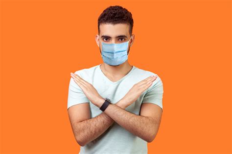 아니 절대적으로 흰색 티셔츠에 의료 마스크를 가진 결정 된 남자의 초상화는 교차 된 손으로 X 기호를 보여주는 정지를 의미 이것은 끝입니다 20 29세에 대한 스톡 사진 및