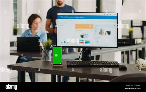Persons Conducting Business Tasks At Agency Workspace With Cellphone Displaying Greenscreen At