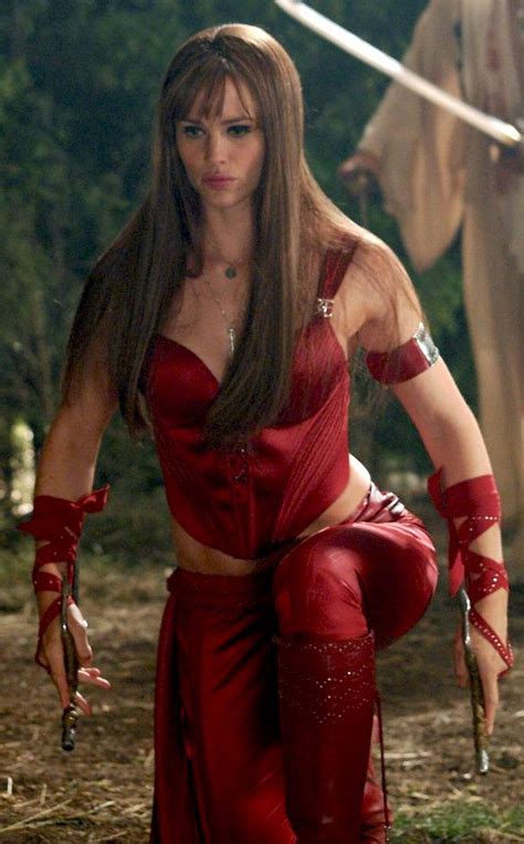 A Woman Dressed In Red Crouching On The Ground With Two Swords Behind