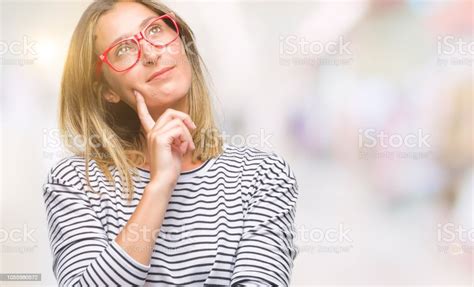 아름 다운 젊은 여자와 함께 고립 된 배경 위에 안경을 착용 질문 잠겨있는 표현에 대 한 생각 하는 턱에 손을 사려깊은 얼굴 미소 의심 개념입니다 금발 머리에 대한 스톡