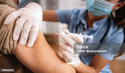 집에서 앉아서 코로나 발병 중에 노인에게 주사를 주는 보호 얼굴 마스크를 가진 간호사를 클로즈업하십시오 백신접종에 대한 스톡