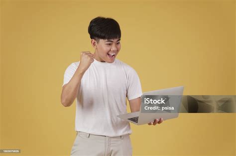 노란 배경에 고립 된 주먹 승자 제스처를하고 캐주얼 들고 노트북 컴퓨터를 들고 캐주얼 옷을 입고 쾌활한 젊은 아시아 남자의
