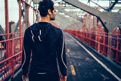 브릿지 서딩 운동에 서있는 스포츠웨어 라벨의 브랜드 이름이 있는 트랙수트를 입은 현대 이어폰의 핏 맨의 뒷모습 윈드 브레이커 재킷을 입은 남성의 뒷모습과 모의 영역 후면에