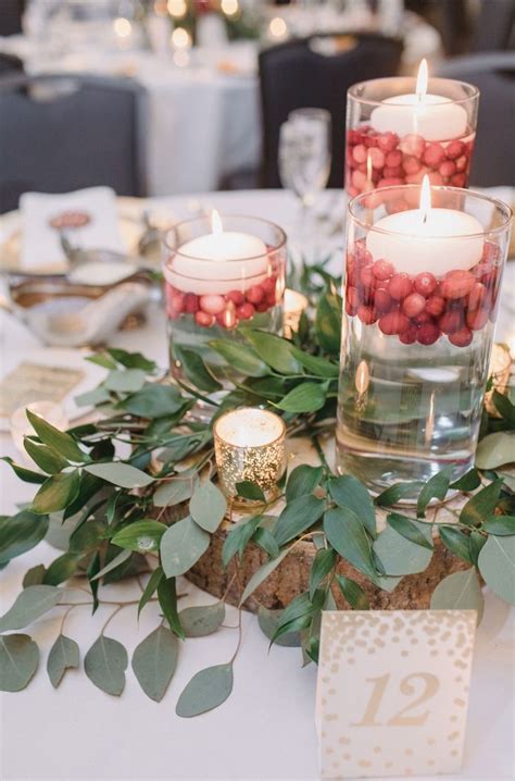 Candles Are Lit On Top Of A Table With Greenery And Berries In Glass Vases