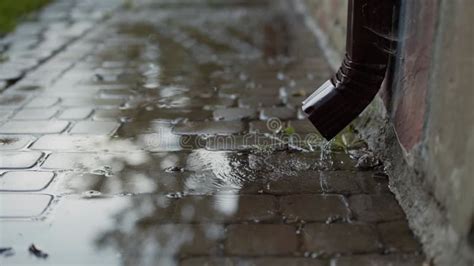 дождевая вода льется из водосточной трубы около дома в плитку сток