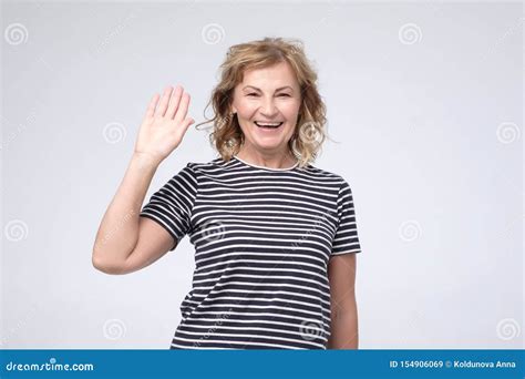 Positive Mature Caucasian Woman Smiling Friendly And Waving Hand At