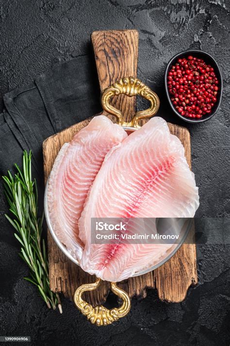 허브와 프라이팬에 틸라피아 물고기의 원시 필레를 요리 할 준비가 검은 색 배경 위쪽 보기 뼈 없는 부드러운 살에 대한 스톡 사진