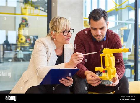 Two Engineers Collaborating On The Design And Functionality Of A Robotic Arm In An Industrial