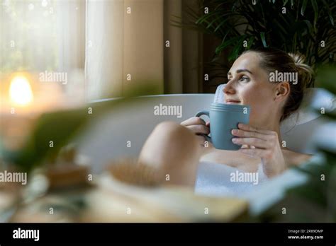 Woman Relaxing In Bath And Drink A Coffee At Home Bathroom Looking Out