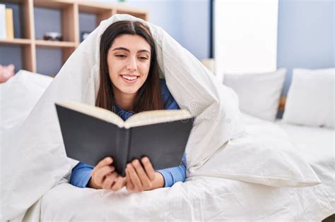 Young Beautiful Hispanic Woman Reading Book Lying On Bed At Bedroom