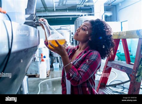 Young Woman In Brewery Filling Flask With Beer From Fermentation Tank