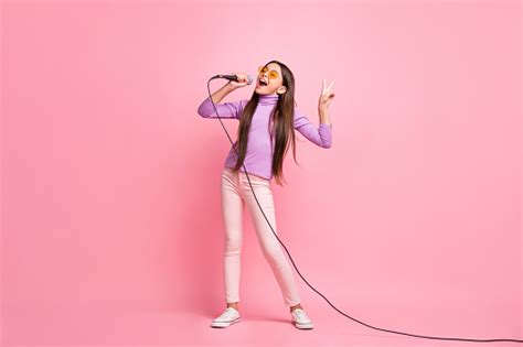 파스텔 컬러 배경에 고립 된 보라색 스웨터를 입고 노래 마이크를 노래하는 작은 아이 소녀 팝 스타의 전체 길이 사진 아이에 대한