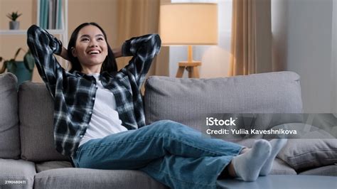 Calm Happy Tired Asian Woman Housewife Resting On Soft Couch Holding