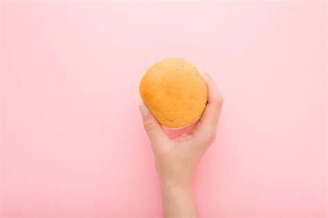 밝은 분홍색 테이블 배경에 신선한 도넛을 들고있는 젊은 성인 여성 손 파스텔 색상 근접 촬영 달콤한 스낵 하향식 보기 개인적
