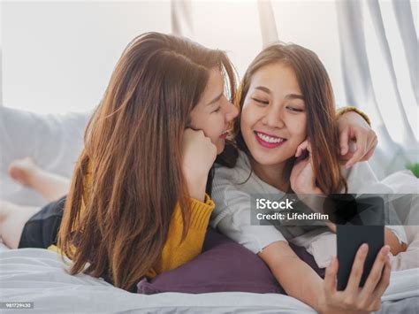 젊은 아시아 여자 레즈비언 커플의 가정에서 침대에 행복 미소 사용 하 여 스마트 폰 자화상 걸릴 사진 라이프 스타일 여성 커플