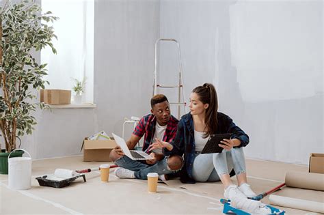 인테리어 디자이너 건설 관리자 건축가는 커피 노트북 태블릿 계획의 머그잔바닥에 앉아 새로 지어진 아파트 건물 아파트 개조 젊은 여성과 동료에서 작업 2명에 대한 스톡 사진