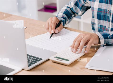 Partial View Of Businessman Making Calculations At Workplace With Documents And Laptop Stock