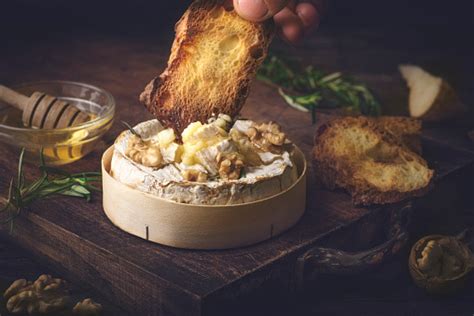 프랑스 치즈 카망베르는 꿀 향기로운 허브 및 견과류와 함께 제공되는 나무 상자에 구워졌습니다 한 남자의 손이 구운 바게트를 녹인 치즈에 담근다 프랑스의 맛 소박한 스타일