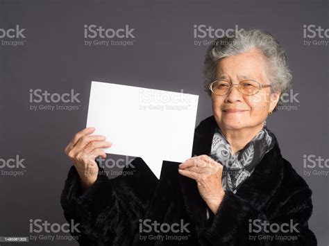 스웨터를 입은 나이든 아시아 여성이 빈 말풍선을 들고 회색 배경에 서서 미소를 지으며 카메라를 바라보고 있다 70 79세에 대한
