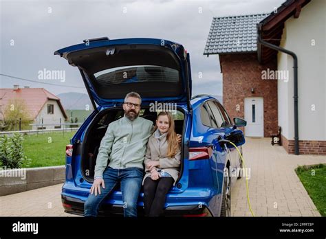 Father And His Daughter Waiting For Charging Their Electric Car Stock