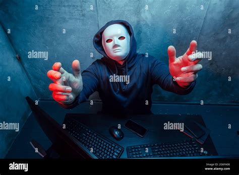 Anonymous Hacker Wearing Face Mask Working On Computer In Dark Room