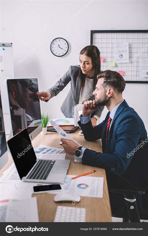 Data Analyst Pointing Computer Monitor Colleague Holding Paper Charts