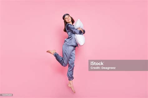 파스텔 핑크 컬러 배경에 고립 된 베개 점프를 포옹하는 잠옷을 입은 소녀의 전체 길이 신체 크기 사진 베개에 대한 스톡 사진 및
